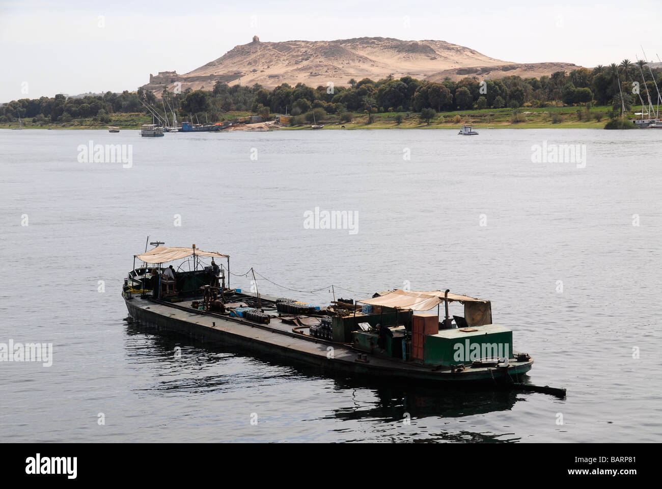 Barge in Aswan, Egypt on the River Nile with the tombs of the nobles in ...