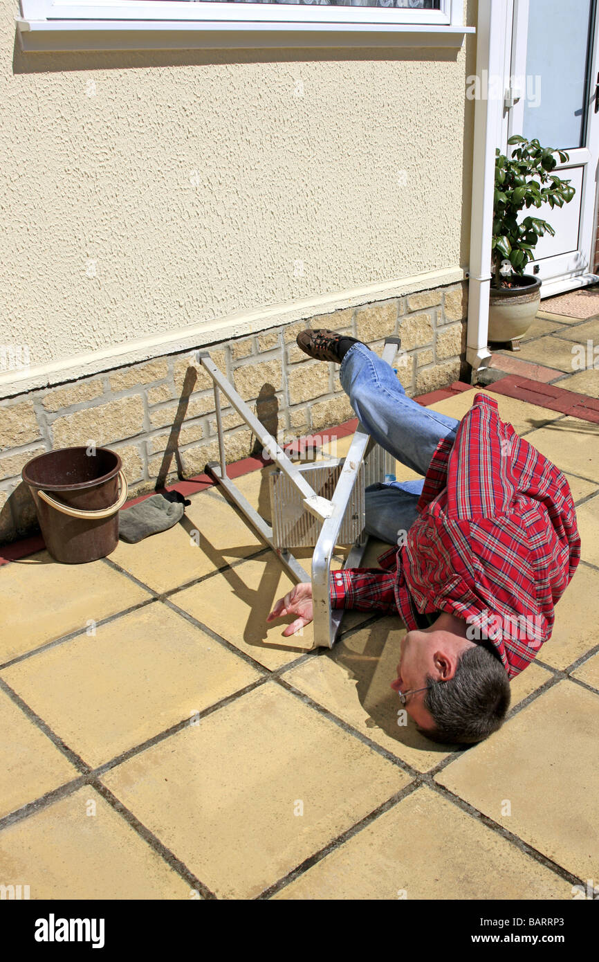 A man having fallen off a step ladder lies injured on a concrete ...