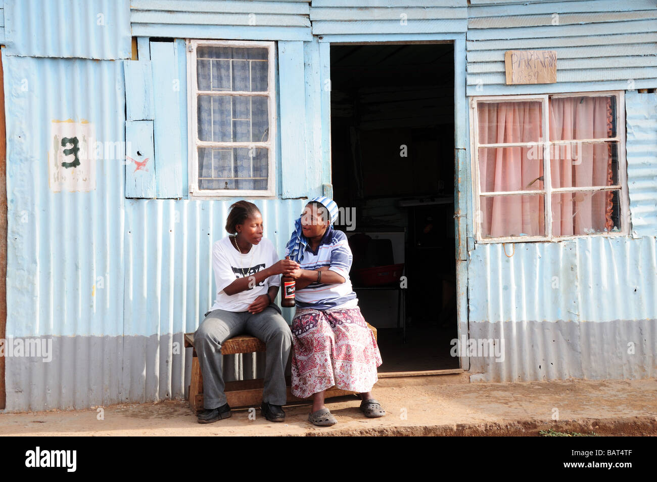Two African women sharing a bottle of beer outside a zinc dwelling ...