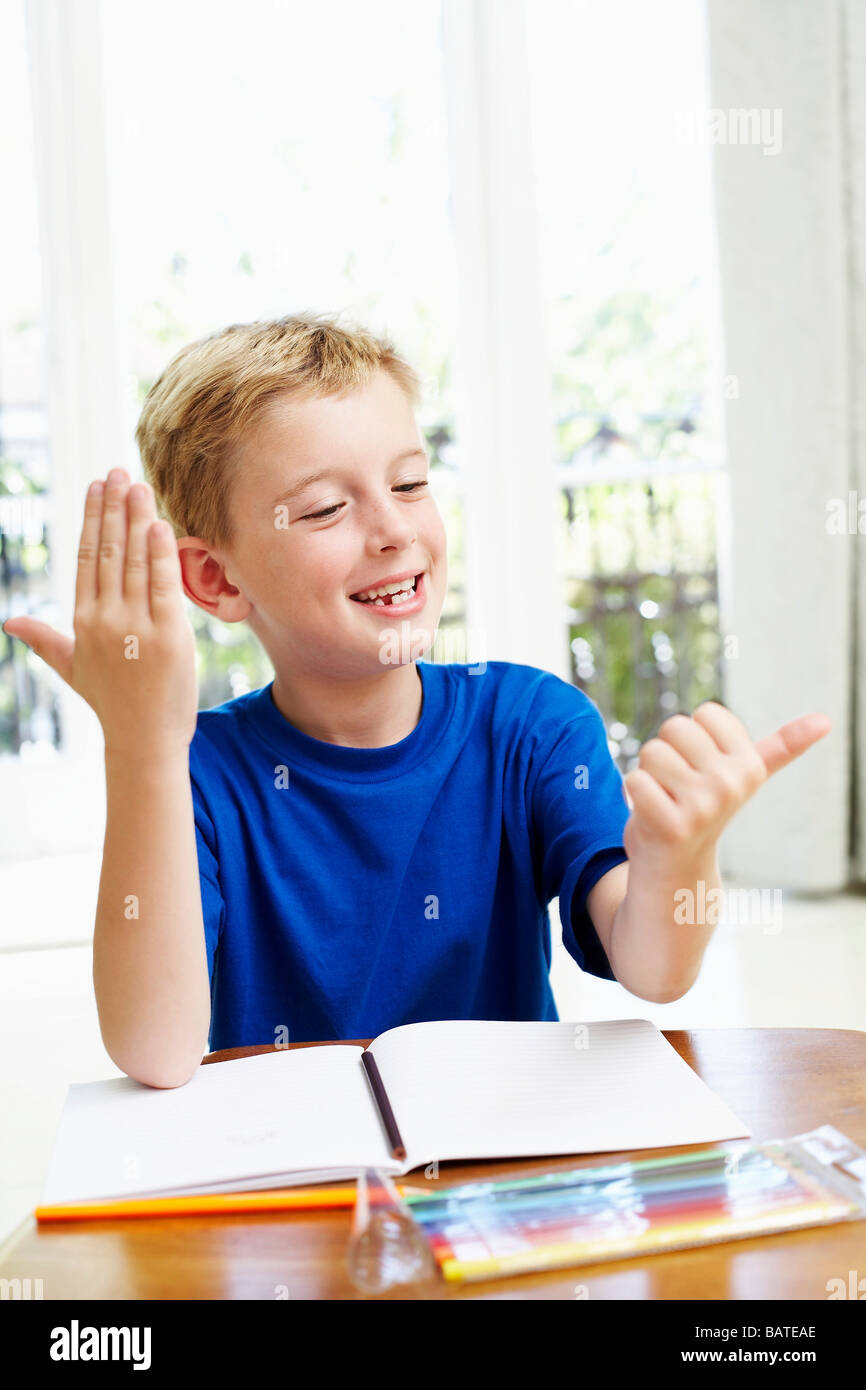 Boy counting on his fingers tocomplete his maths homework. He is six ...