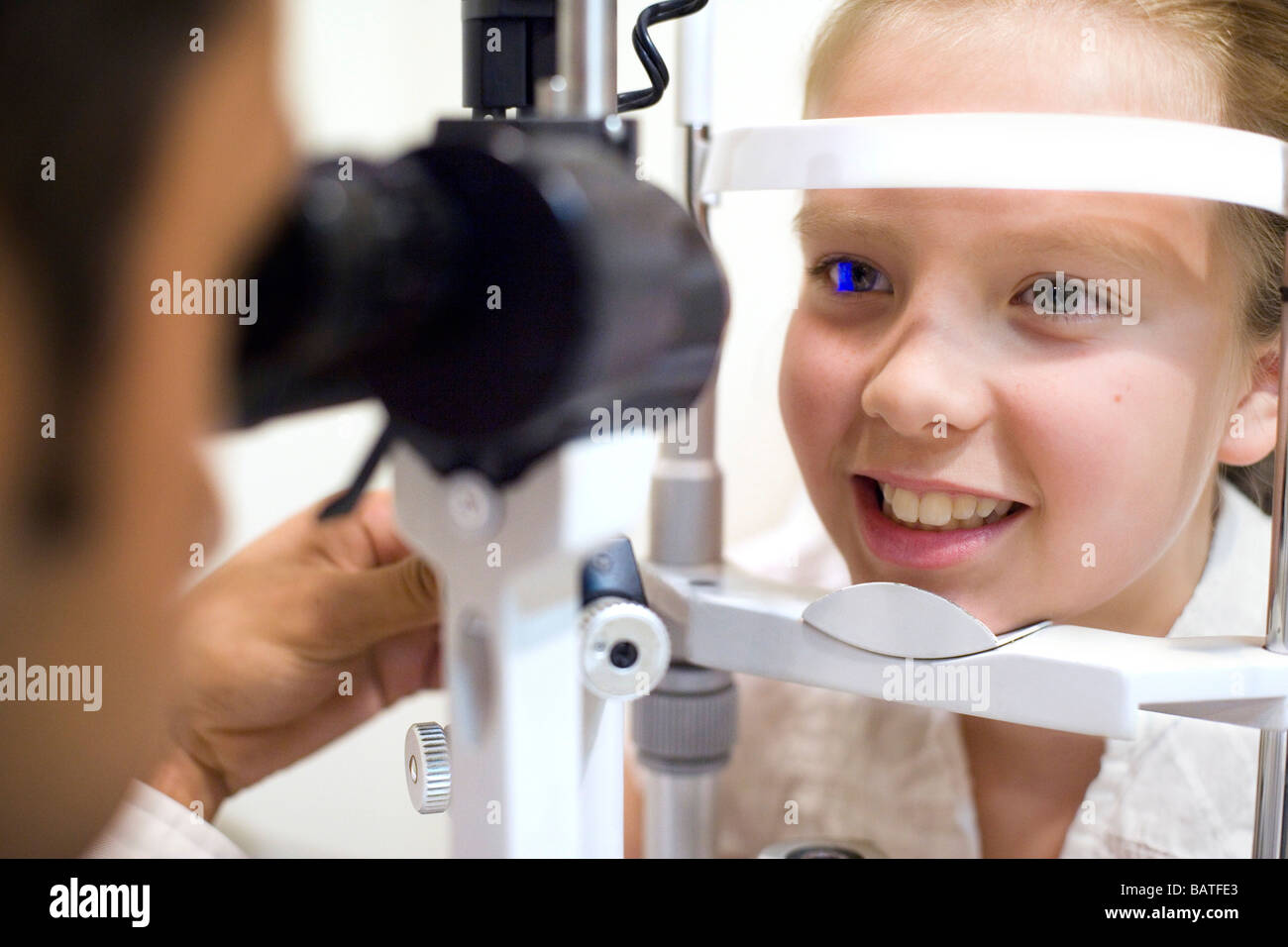 Eye examination. Optician using aslit lamp to examine a ten year old ...
