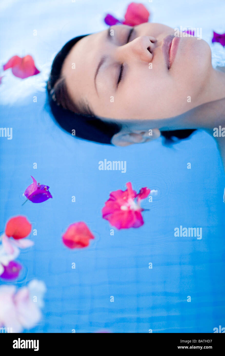 Relaxed woman on holiday, floating in a pool scattered with petals ...