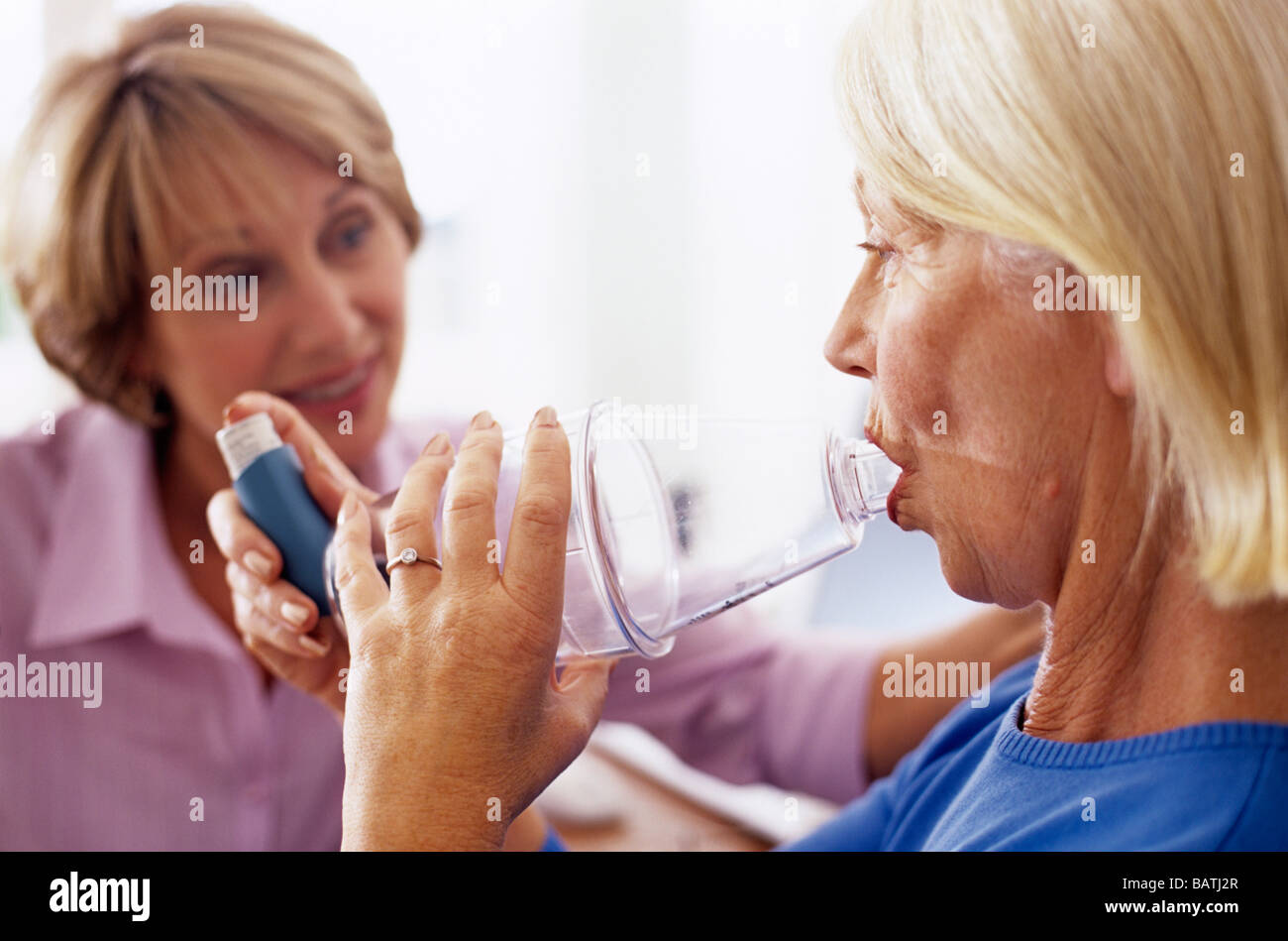 Asthma spacer. 63-year-old woman using a spacer (plastic chamber) with ...