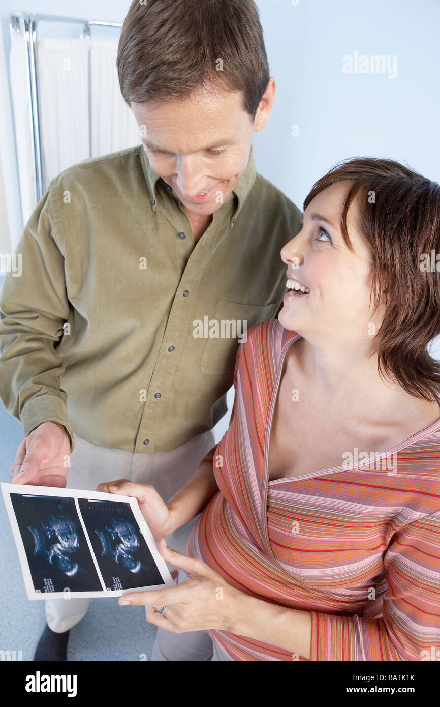 Expectant parents looking at ultrasound scans of their unborn child ...