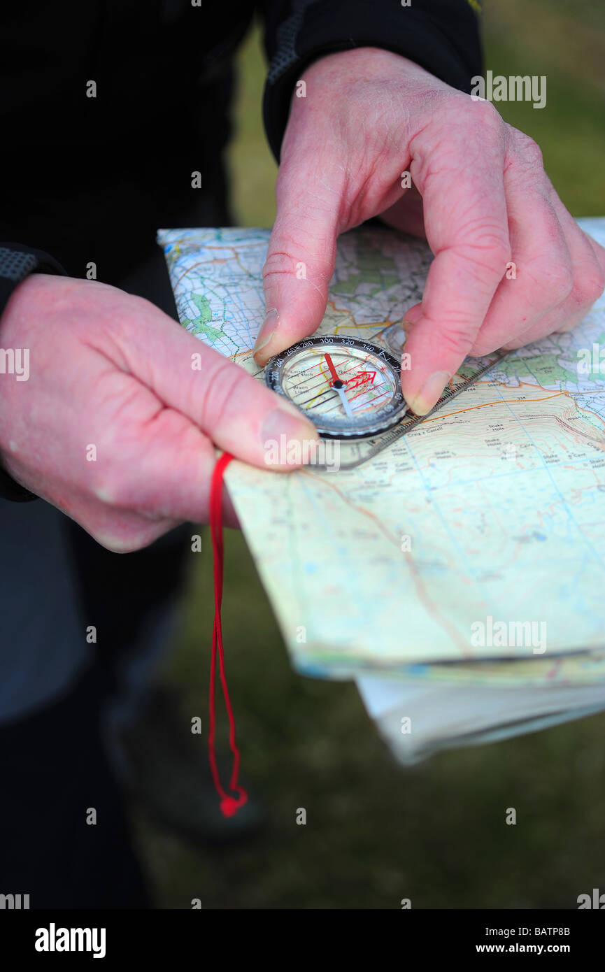 A mans hands holding a map and compass for orienteering and map reading ...