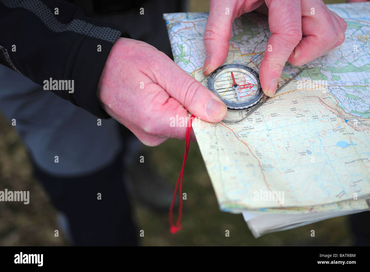 A mans hands holding a map and compass for orienteering and map reading ...