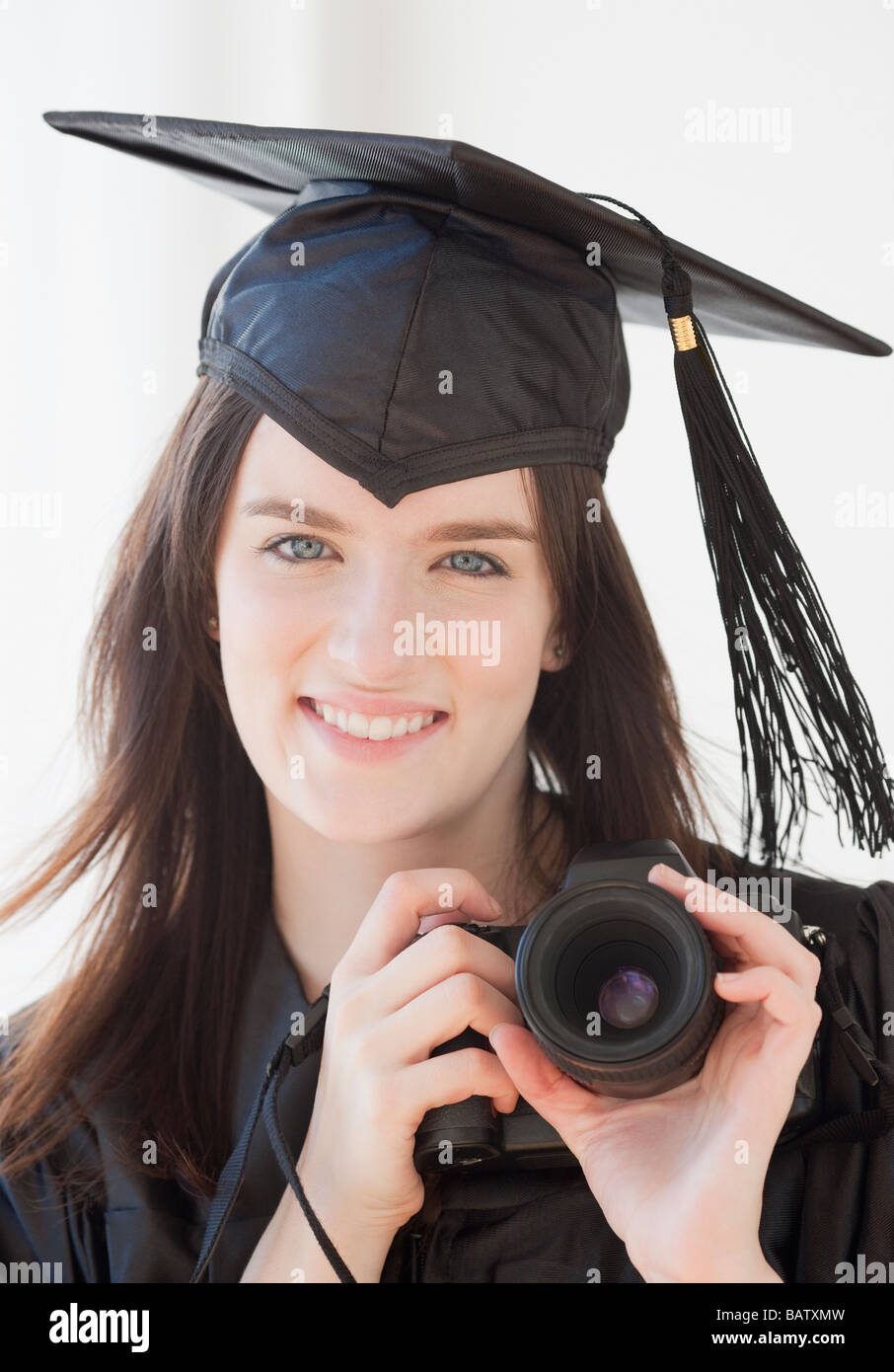 Portrait of young woman in graduation gown holding camera Stock Photo ...