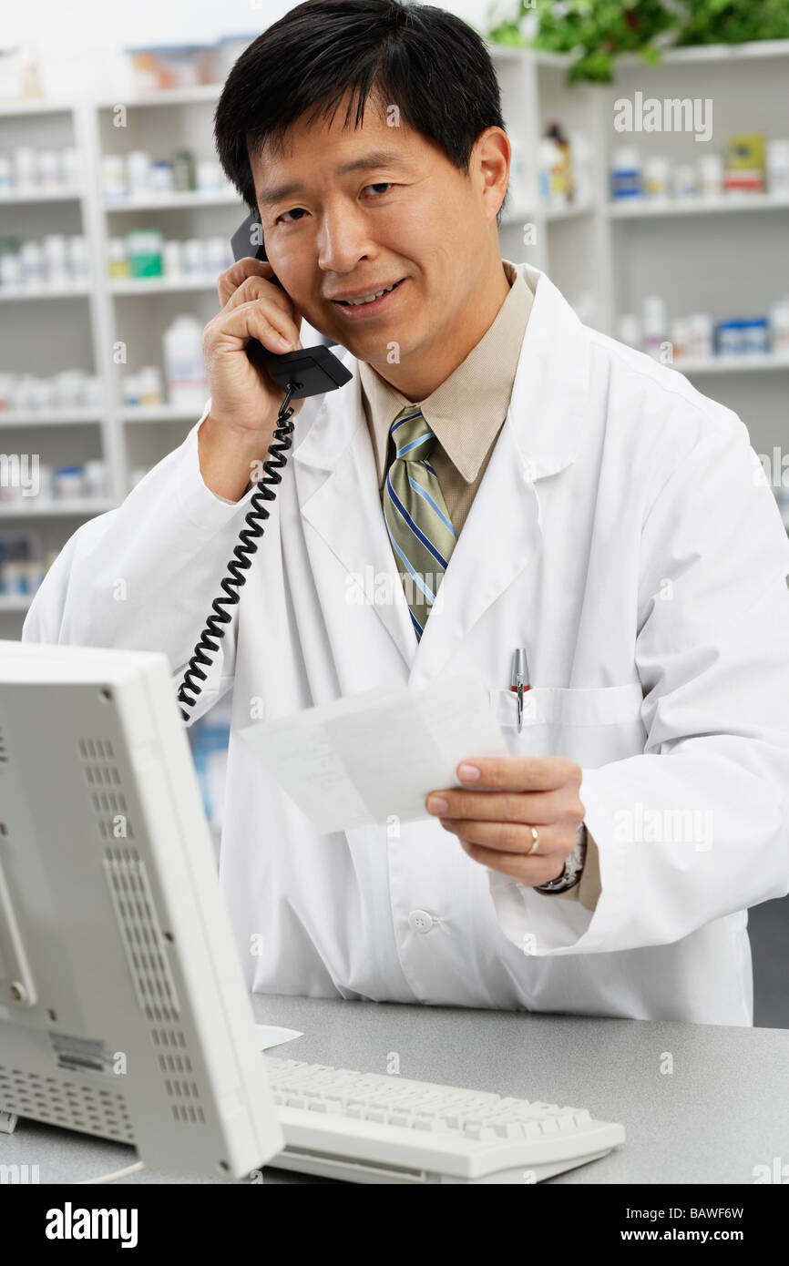 Asian male pharmacist talking on telephone Stock Photo - Alamy