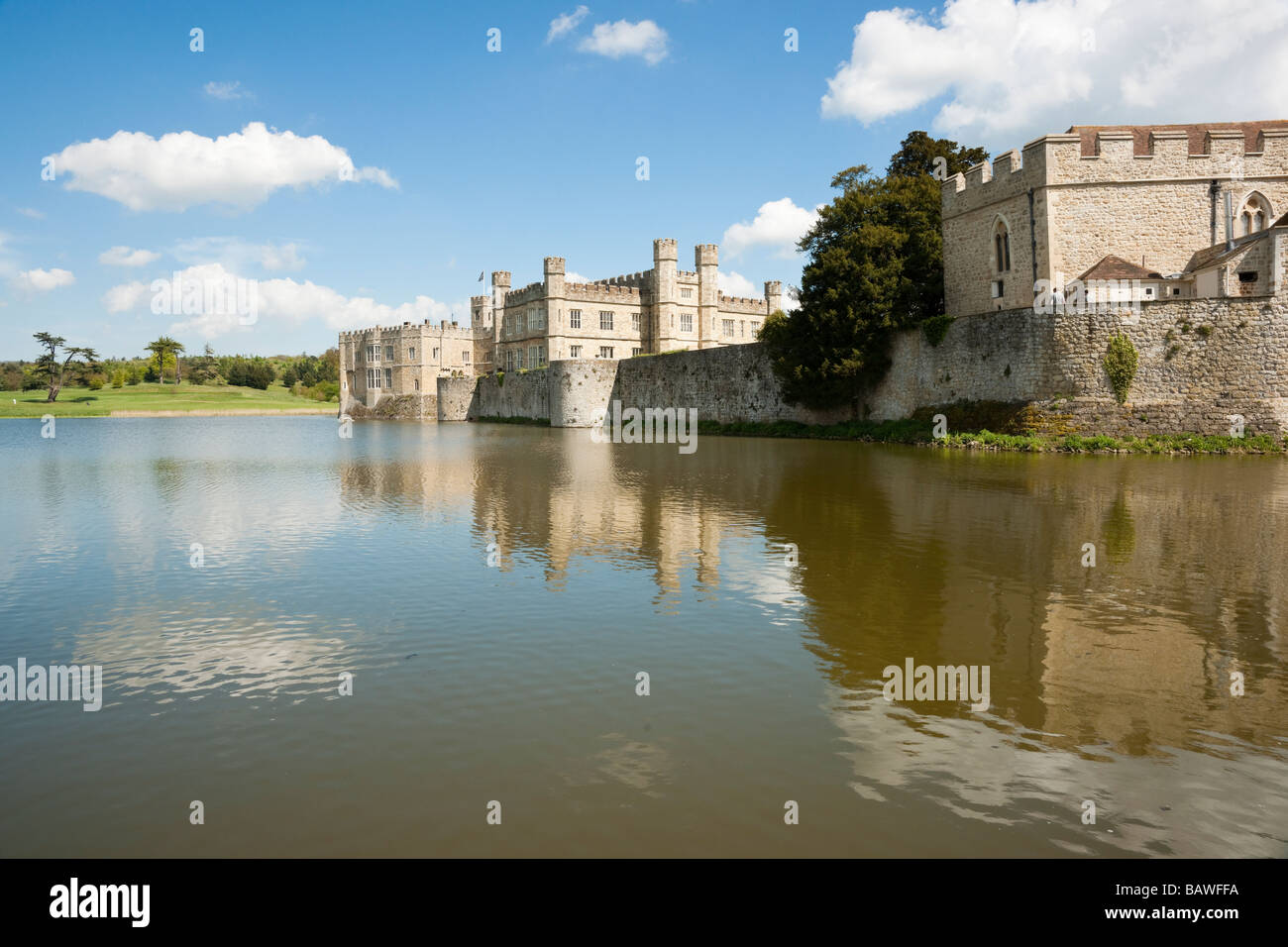 Castle and reflection on lake or mote against blue sky with clouds ...