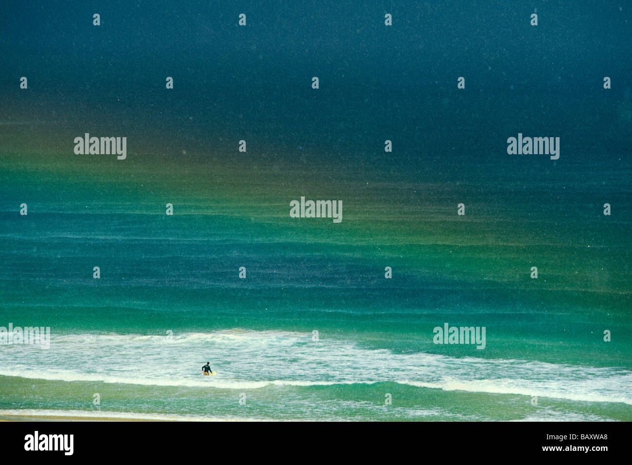 Lone surfer under a rainbow in severe rain storm at iconic Bondi Beach ...