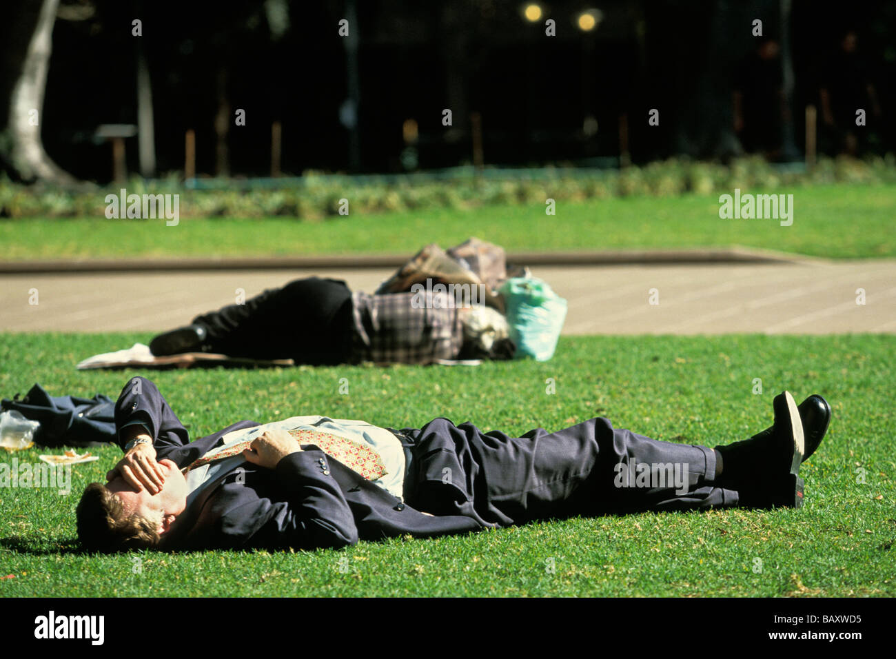 Businessman and homeless person resting in the sun at Hyde Park in the ...