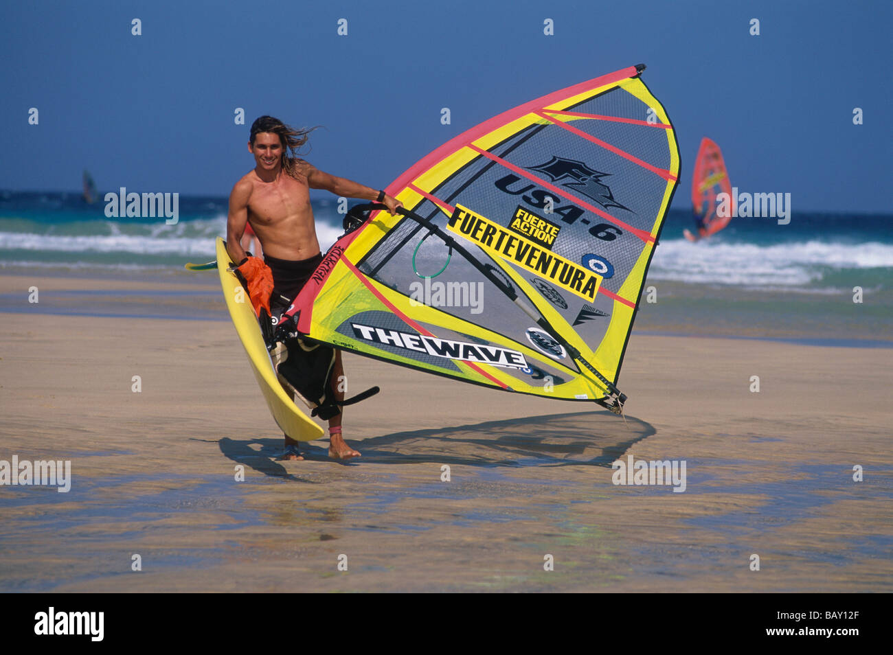 Athletic sailboarder holding his board and sail at the beach Playa ...