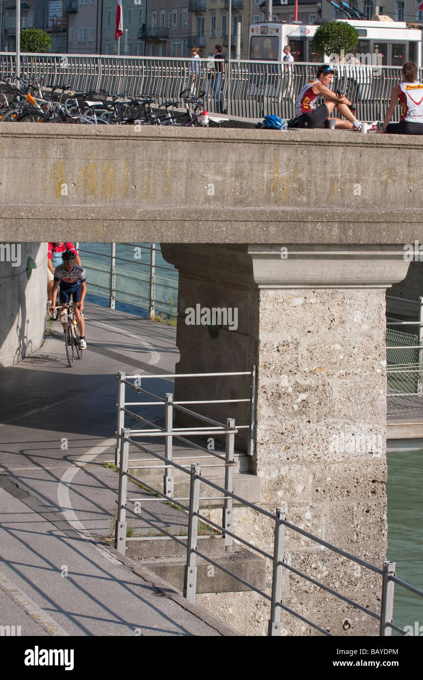 A cyclist rides under a concrete bridge along a riverside path, while ...