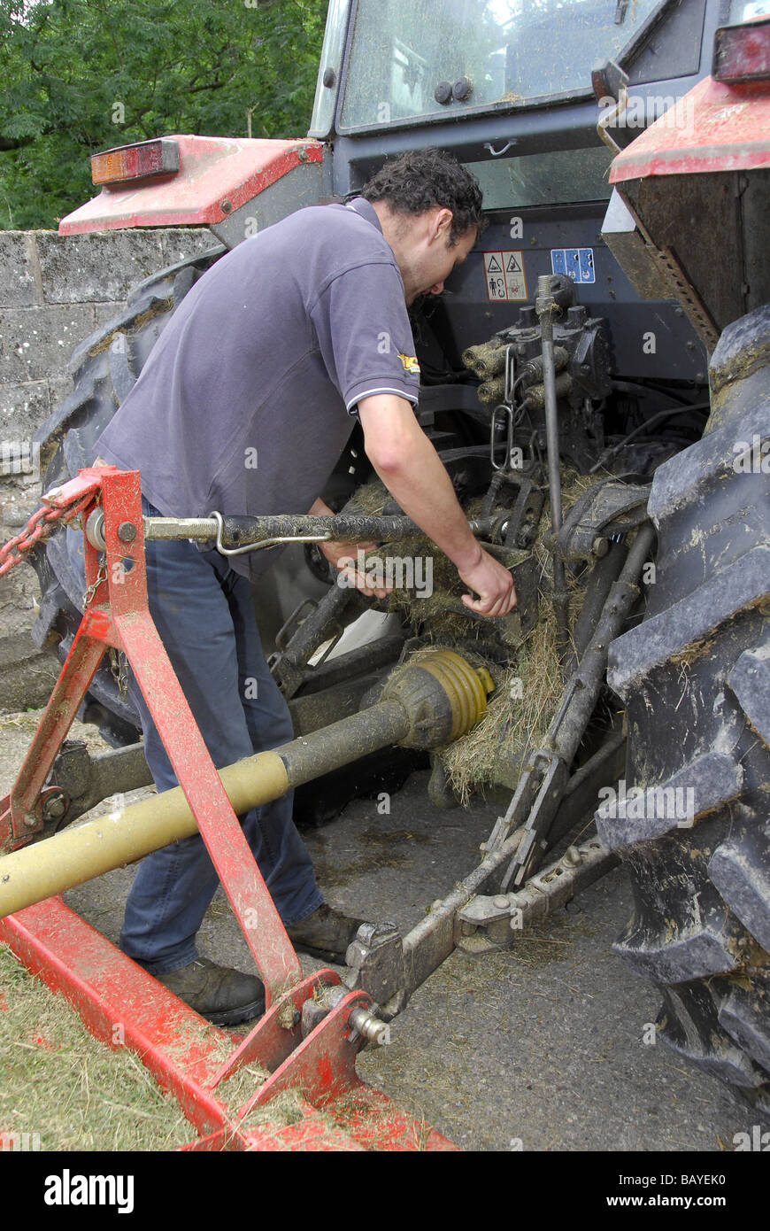Farmer securing grass cutting machinery onto the back of a red farm ...