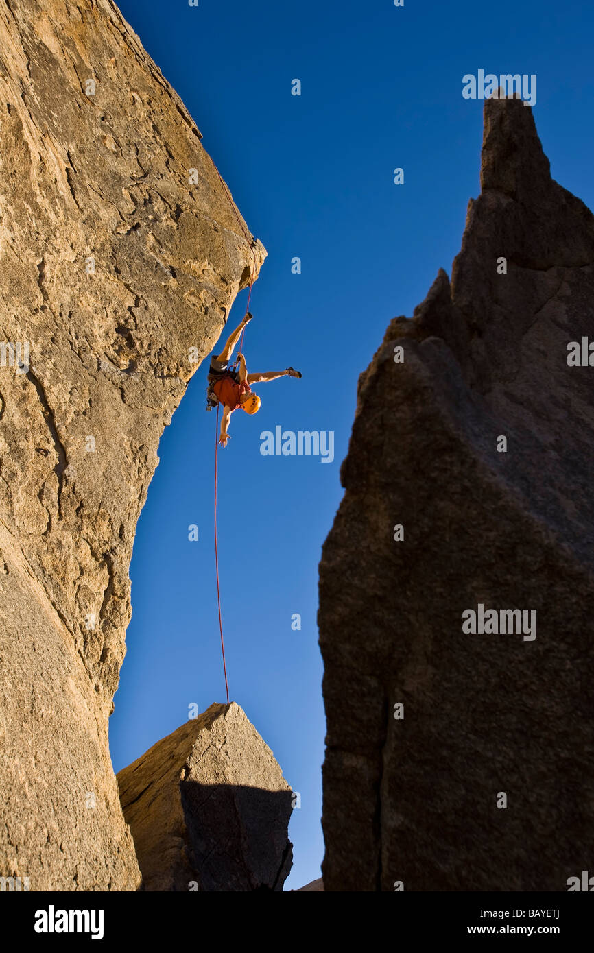 Rock climber dangling in mid air after rappelling past an overhang ...