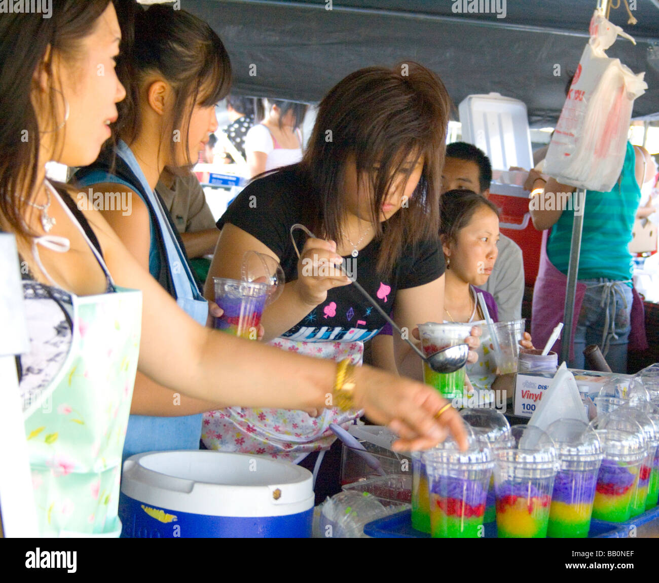 Attractive teenage Hmong SE Asian women fill cups with fruit drink ...