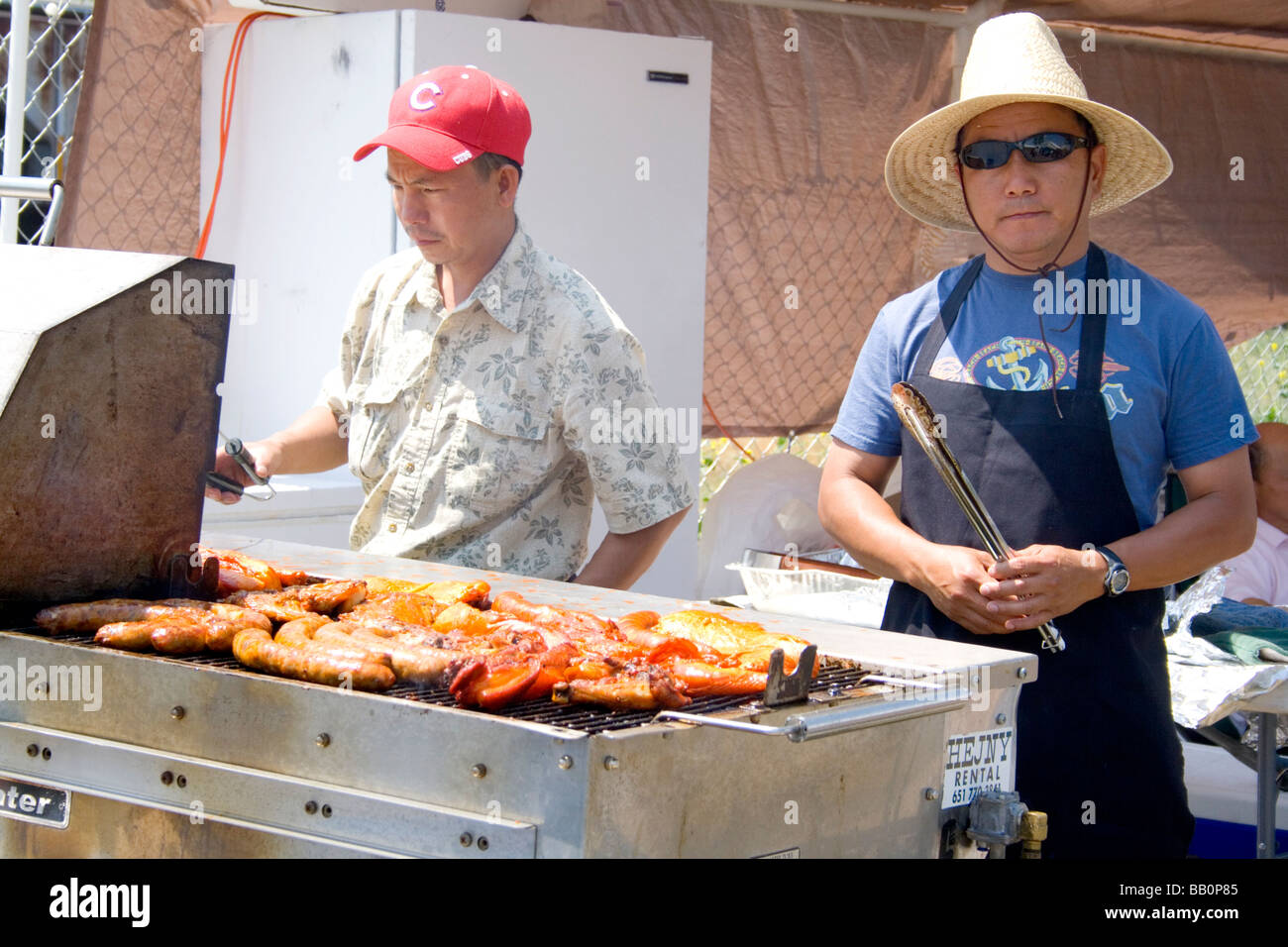 Hmong cooks roasting chicken and sausage for outdoor restaurant. Hmong ...