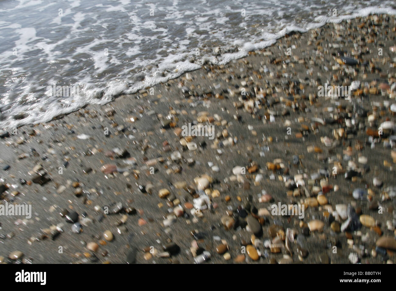 fast flowing ocean wave and sea shells and pebbles washed up on sandy ...