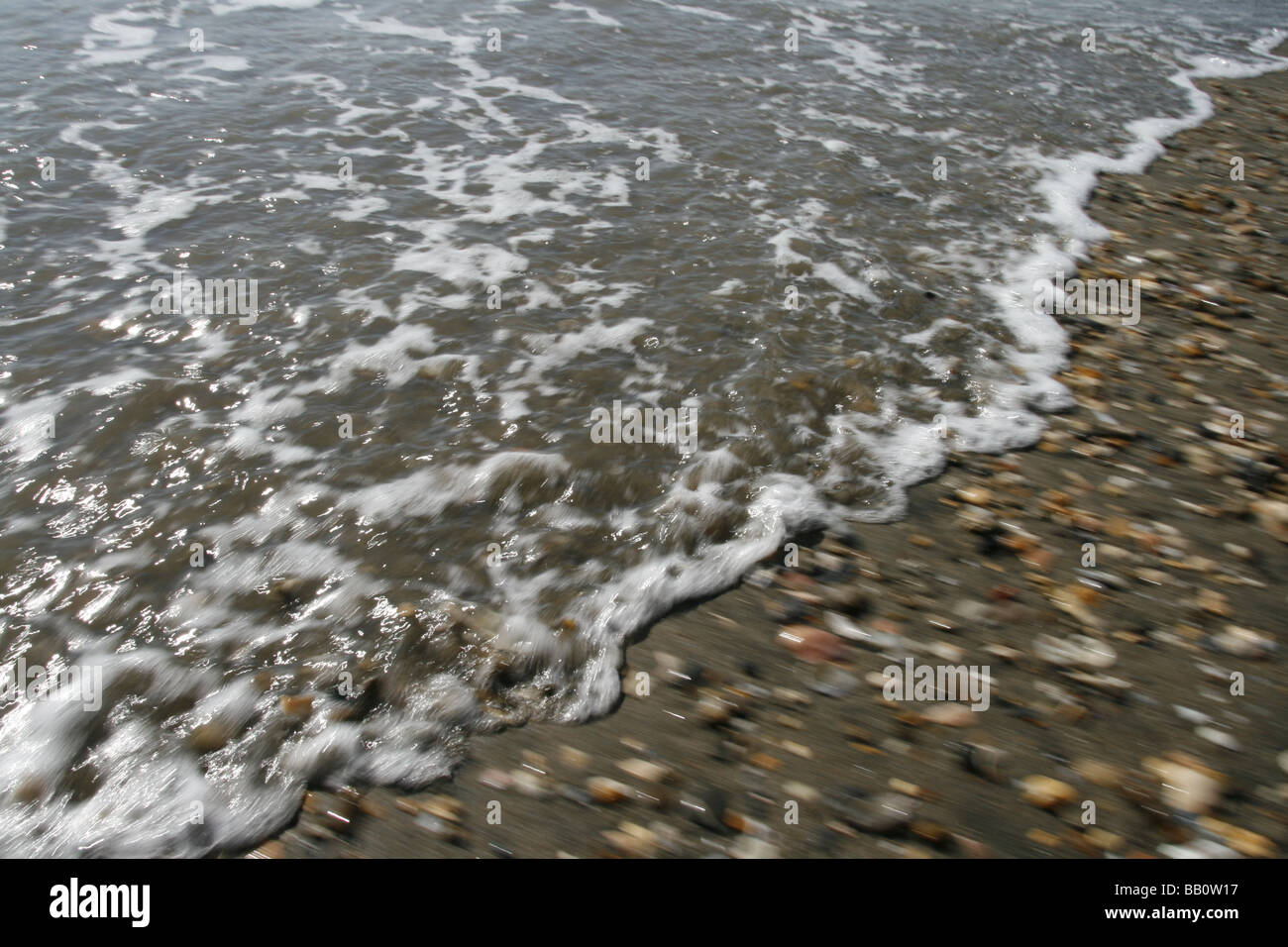 fast flowing ocean wave and sea shells and pebbles washed up on sandy ...