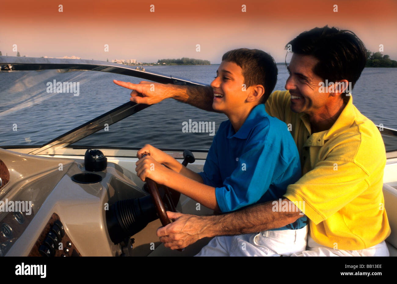 Hispanic father and son sharing the fun of boating and driving the boat ...