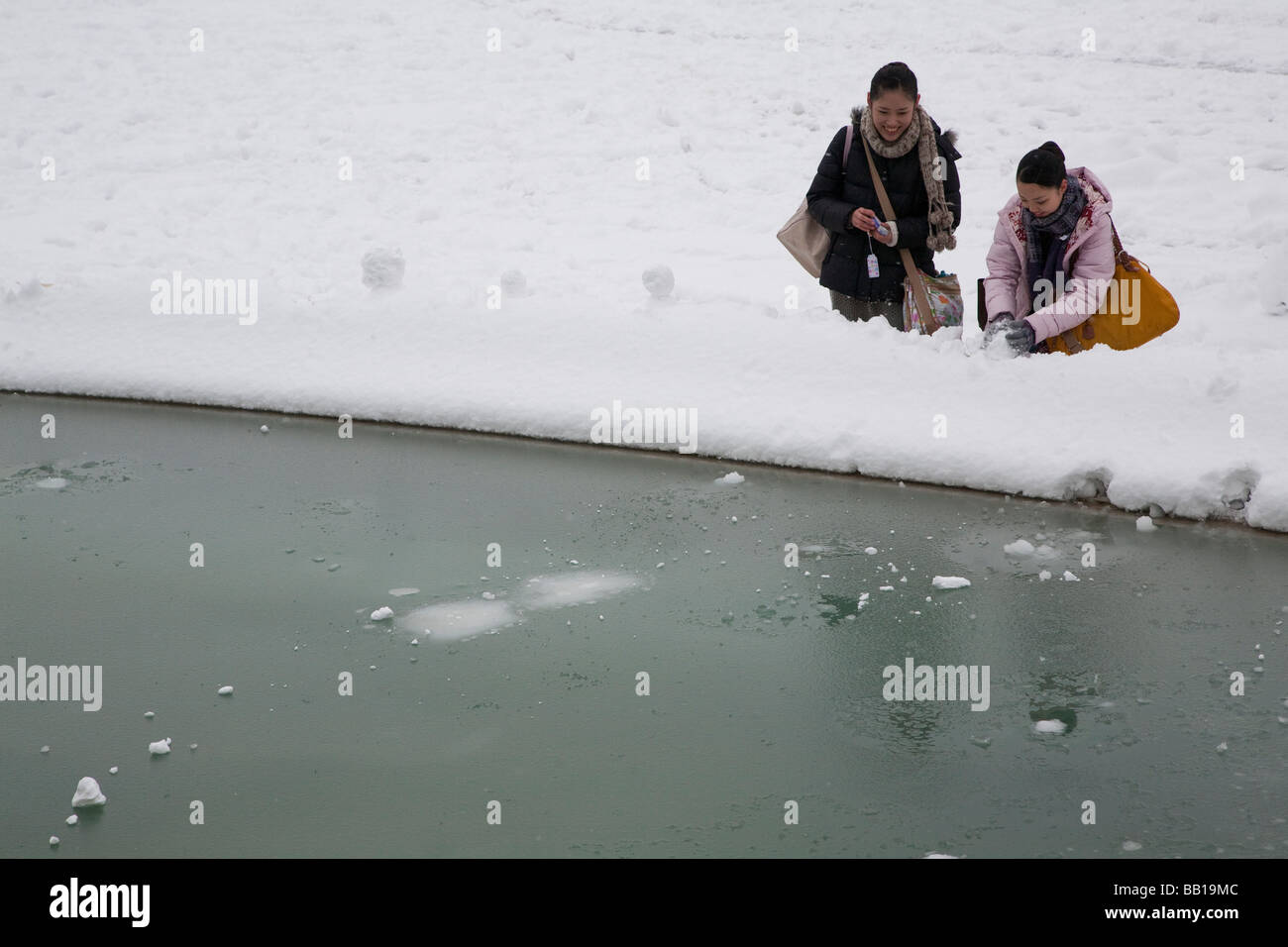 Two young woman making snowballs to throw in fountain Stock Photo - Alamy
