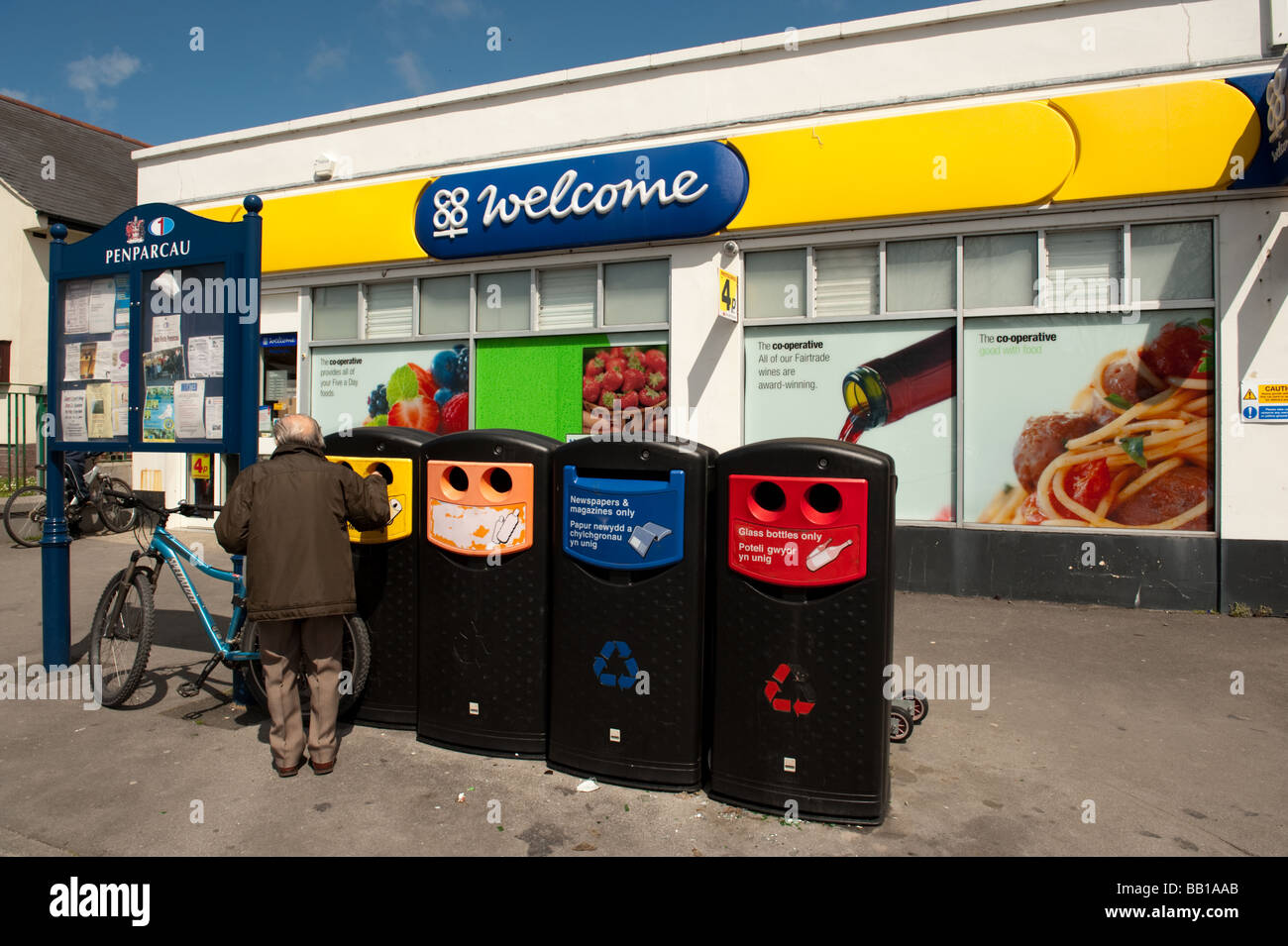 An elderly man recycling tin cans in bins outside a Co Op store ...
