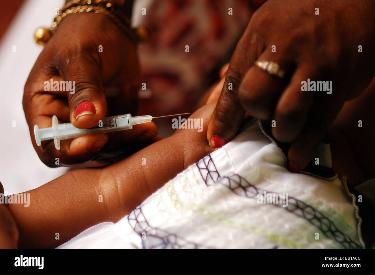 Black hands with flaky red polish on the nails holding a syringe ...