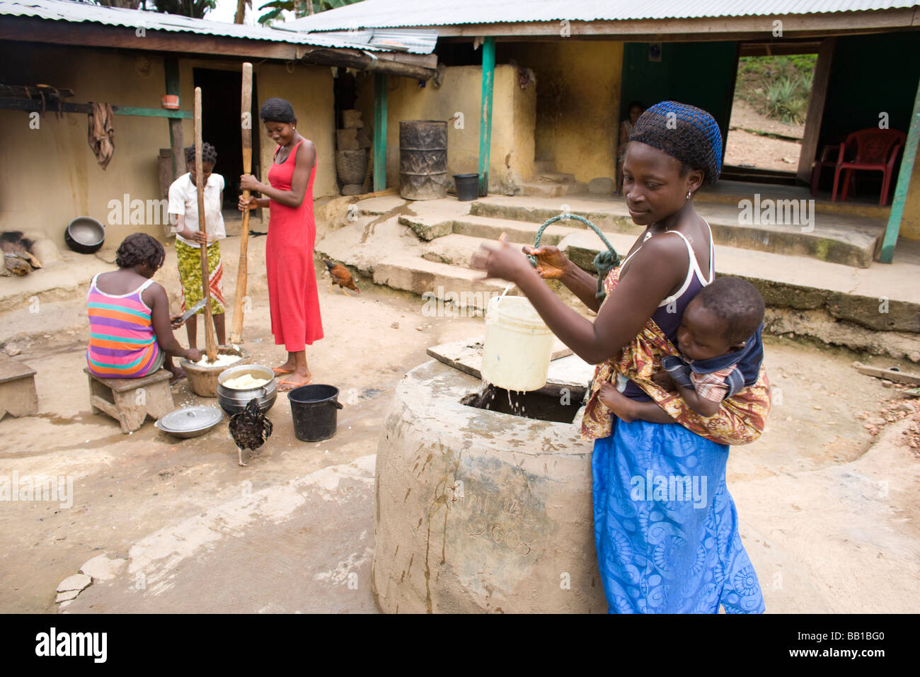 Women preparing food while another woman fetches water from well with ...