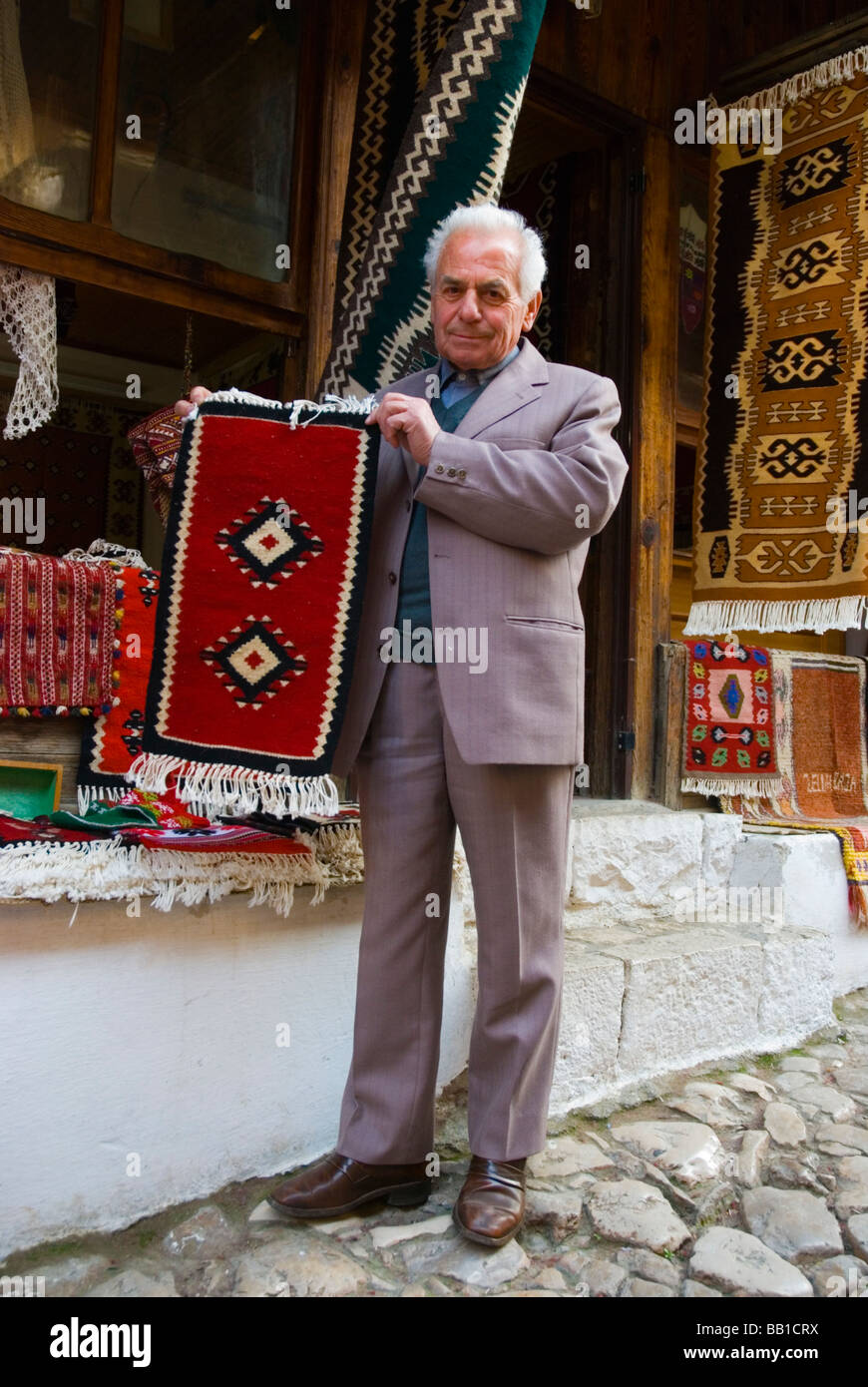 Shopkeeper holding up a traditionally made rug in bazaar of Kruja ...