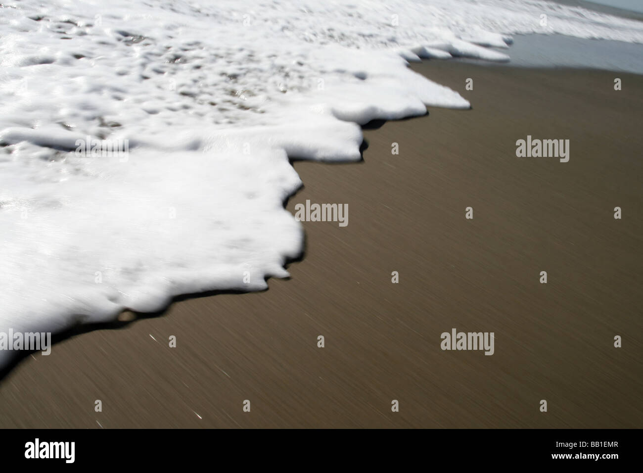 fast flowing ocean wave and sea shells and pebbles washed up on sandy ...