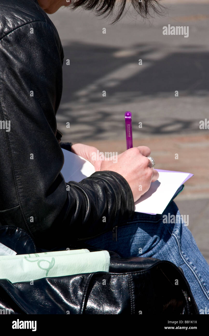 Closeup of a woman wearing a black leather jacket sitting writing on a ...