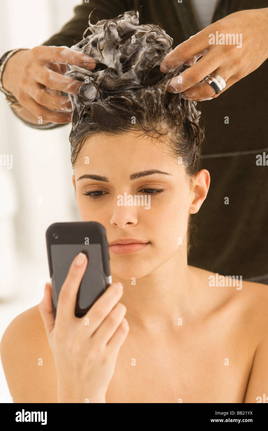 Woman using a mobile phone and having hair washed by a hairdresser ...