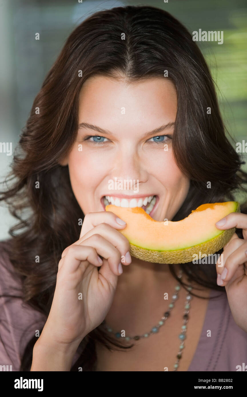 Portrait of a woman biting a slice of cantaloupe Stock Photo - Alamy