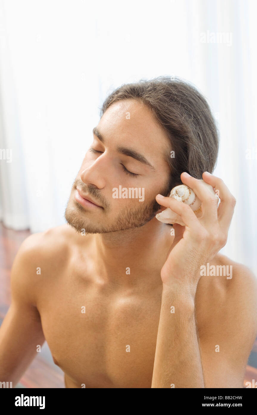 Man holding a conch shell to ear Stock Photo - Alamy
