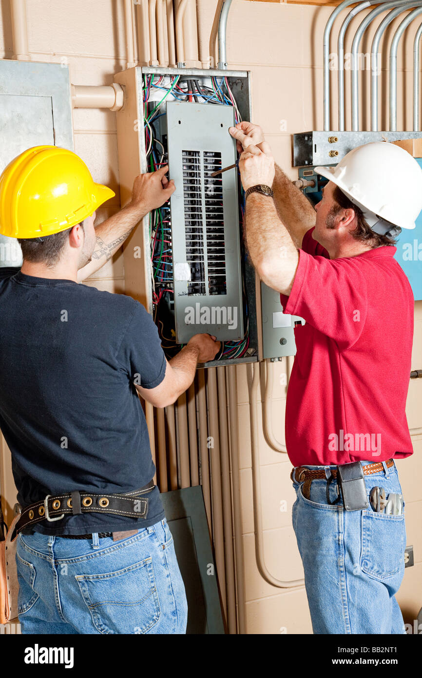 Two electricians repairing an electrical circuit breaker panel in an ...