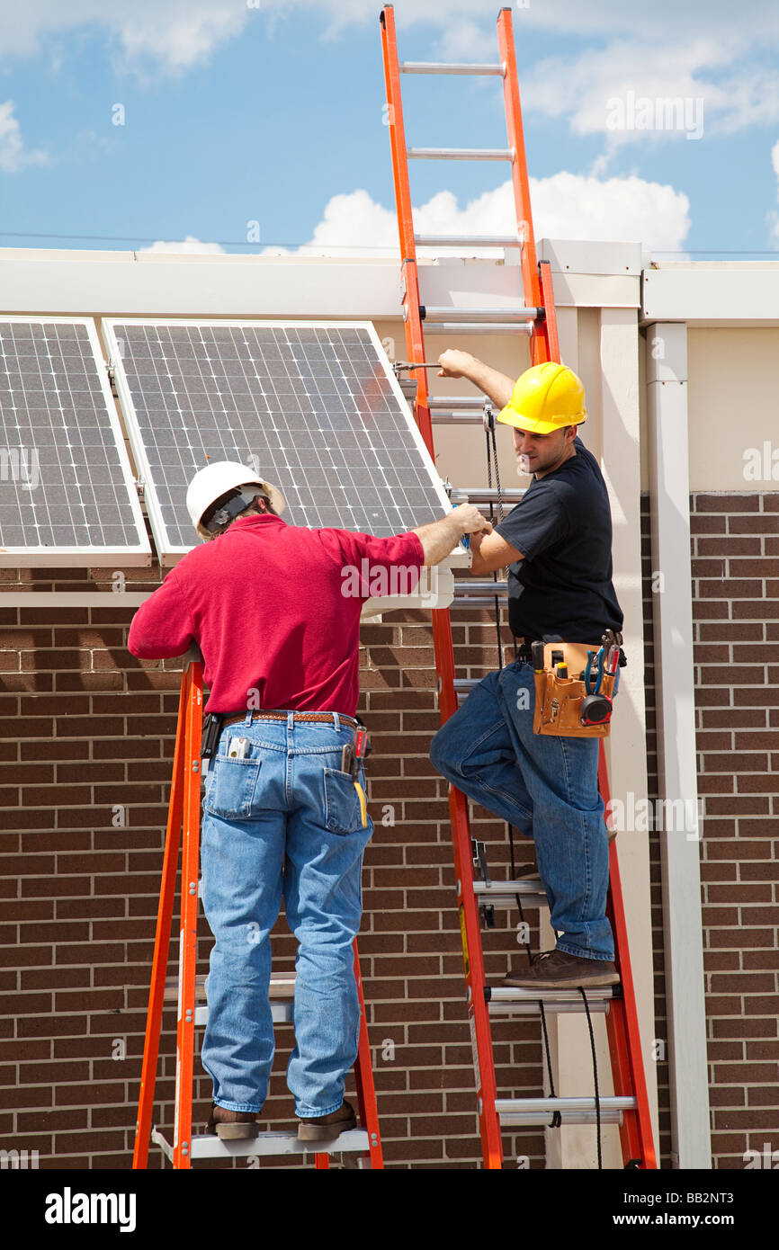 Construction electricians installing solar panels on the side of a ...