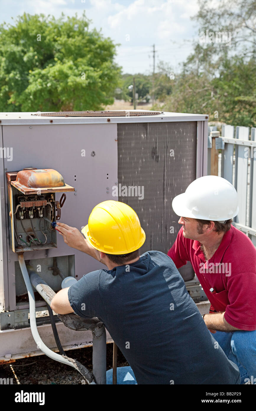 Two AC technicians on a roof repairing an industrial compressor unit ...