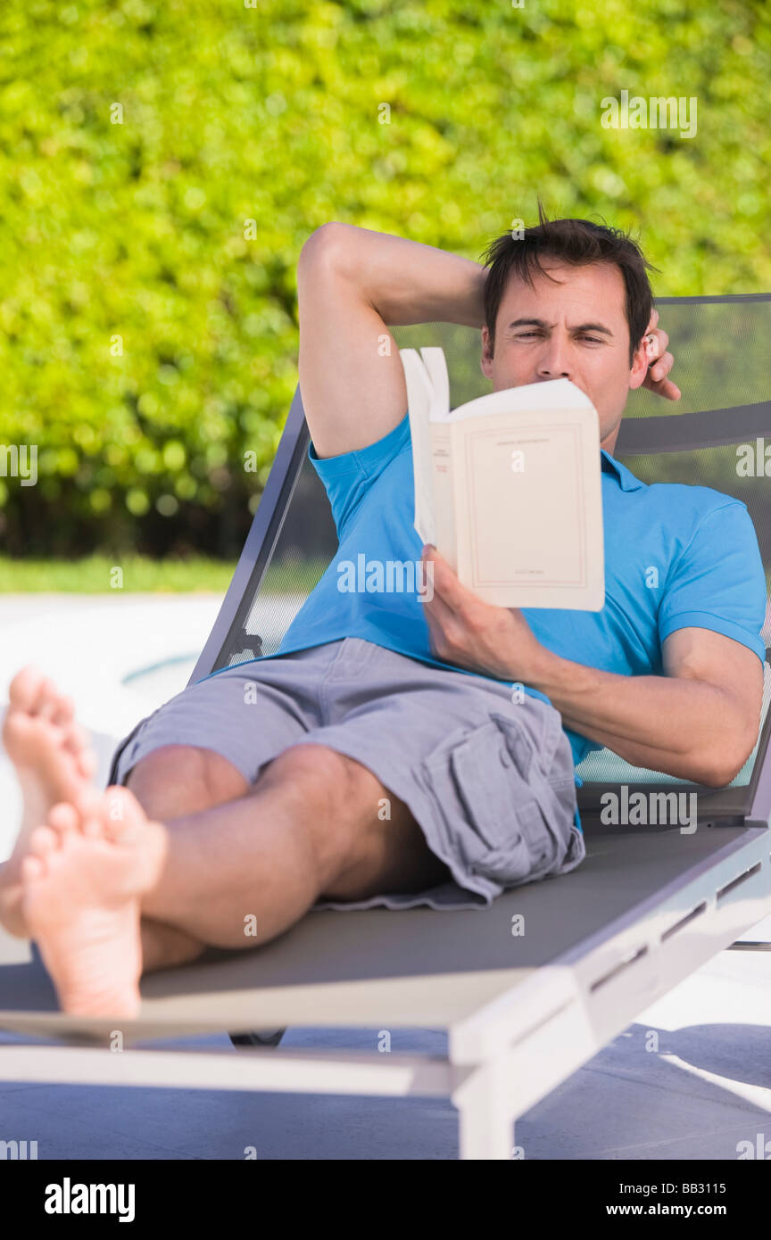 Man reading a book on a lounge chair Stock Photo - Alamy