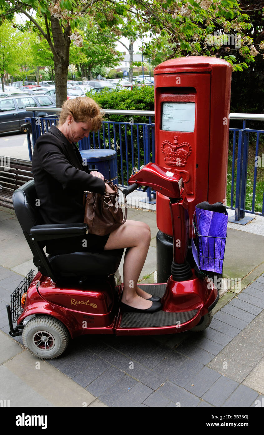 Female mobility scooter driver looking into her handbag at a letterbox ...