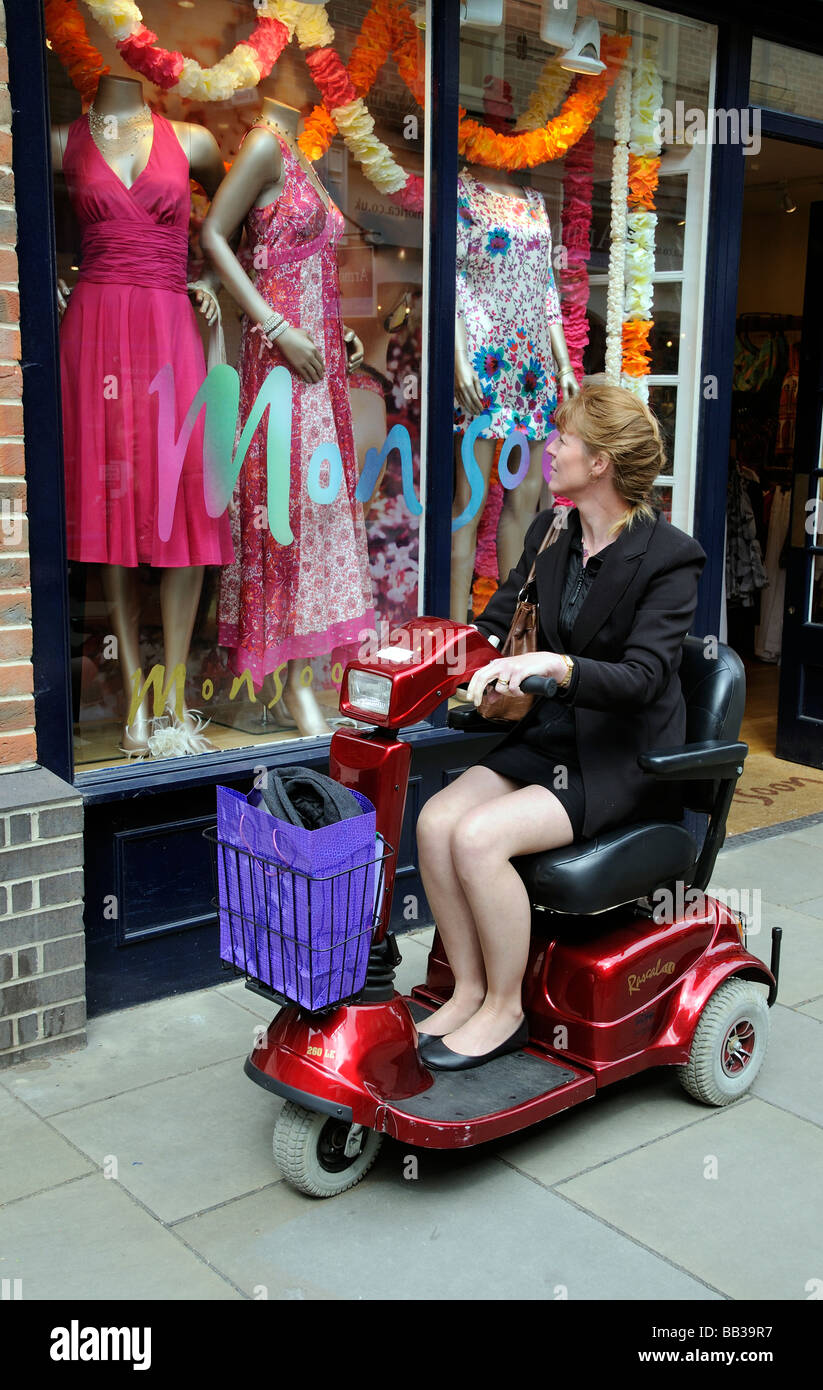 Female mobility scooter driver driving in town centre window shopping ...