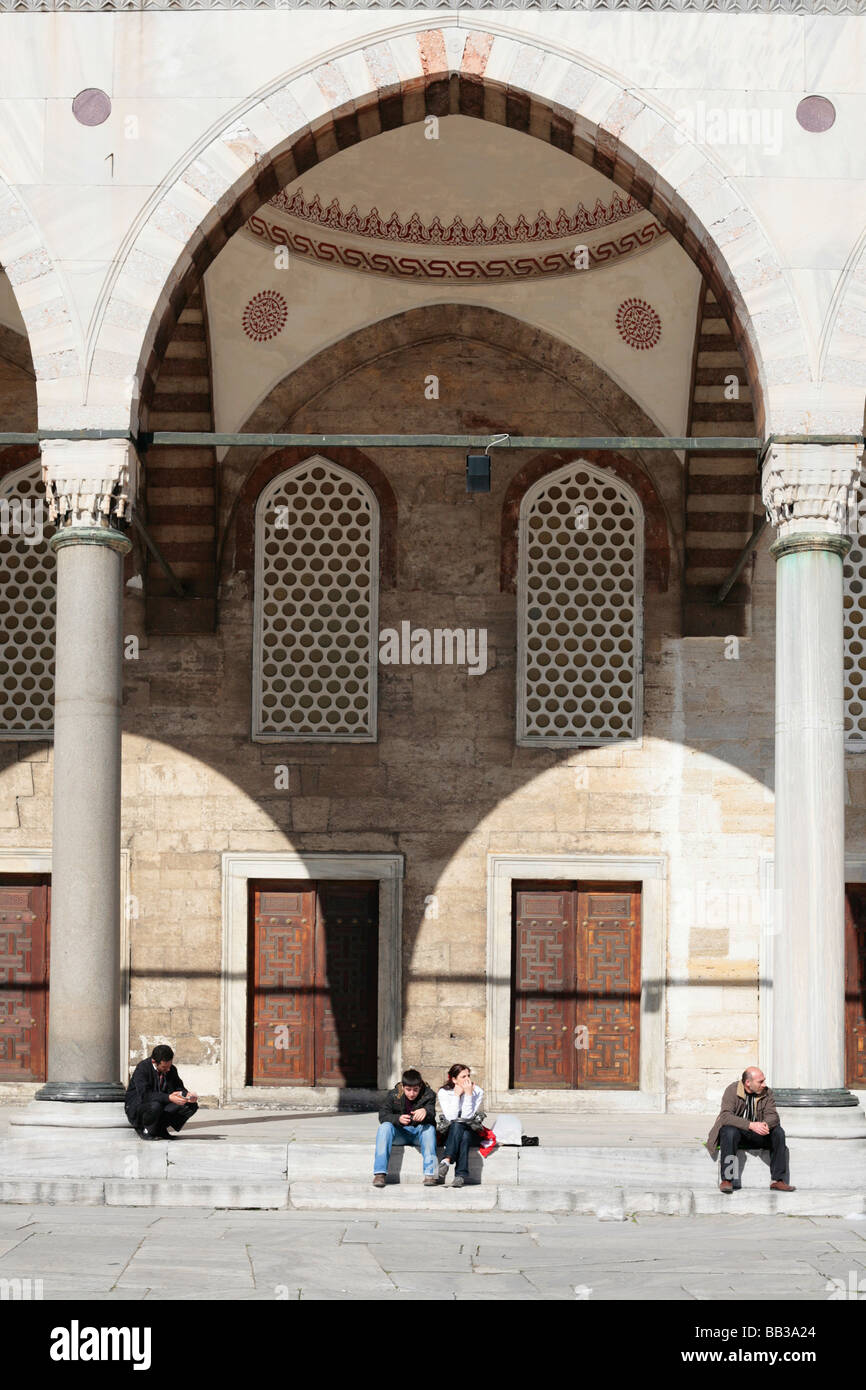 Visitors sitting under one of the arches of the Blue Mosque Courtyard ...