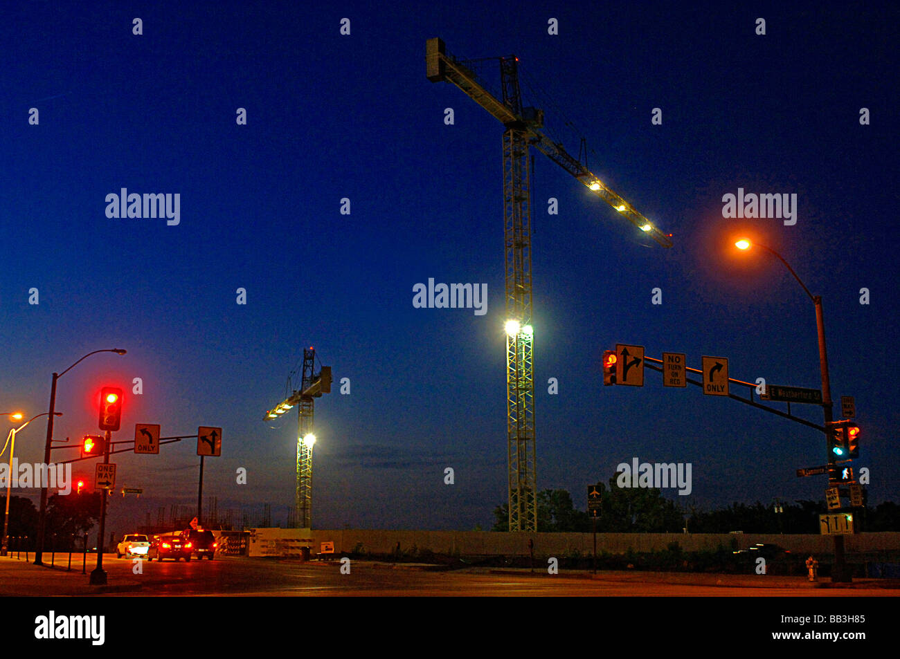 Construction cranes sit idle at twilight, while light traffic and an ...