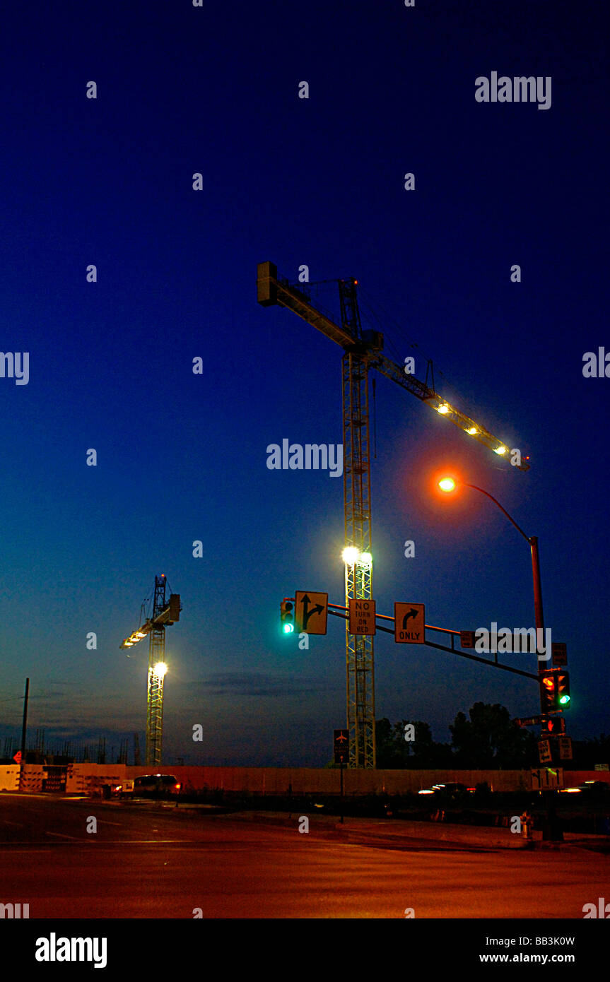 Construction cranes sit idle at twilight, while light traffic and an ...