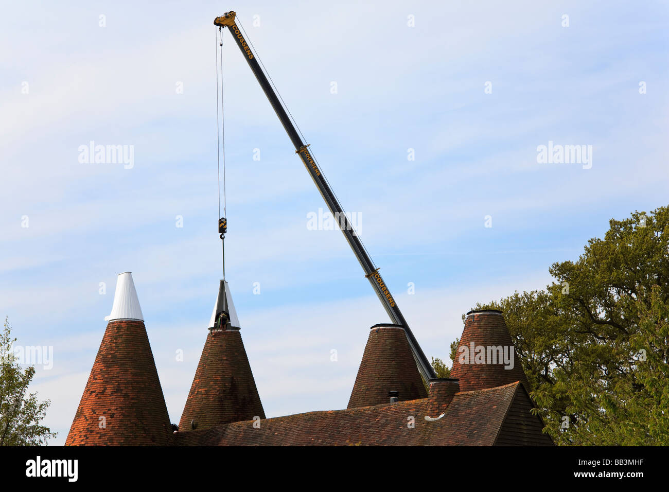 A workman fits a Cowl to the top of a Kent Oast Kent UK A Crane lowers ...