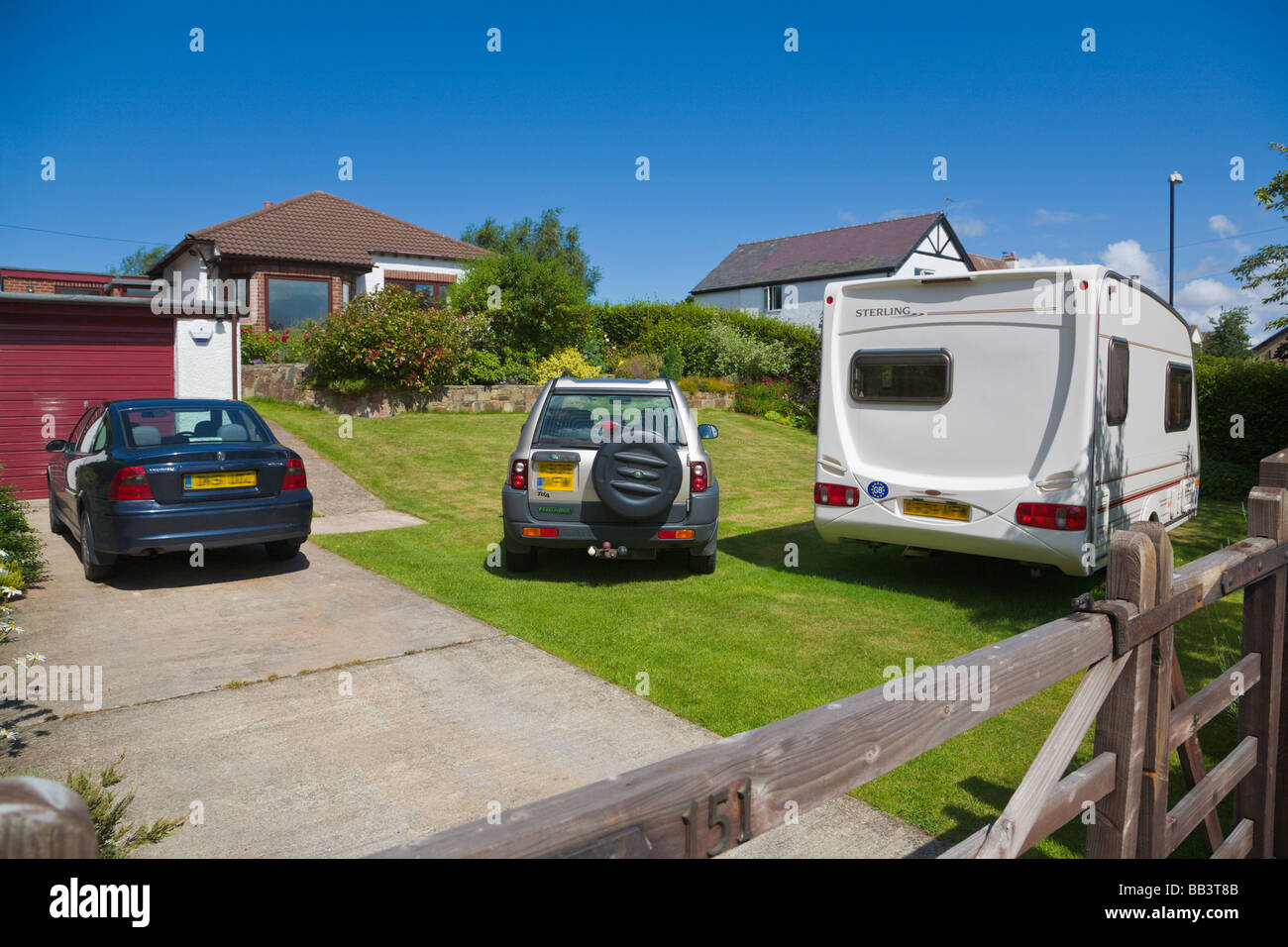 Driveway and garage of detached bungalow with parked cars and caravan ...