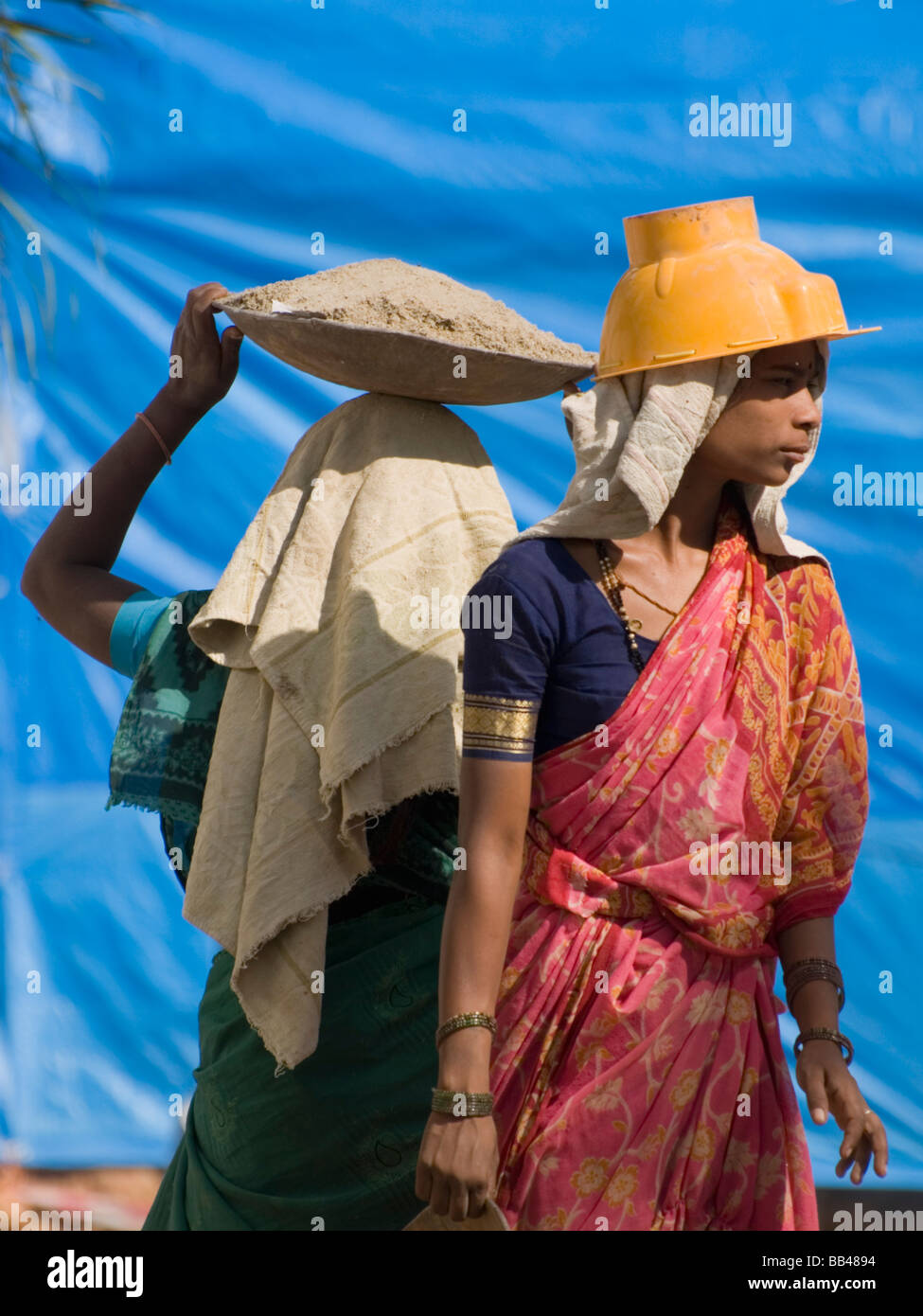 Female workers on a construction site carry cement in steel bowls, on ...