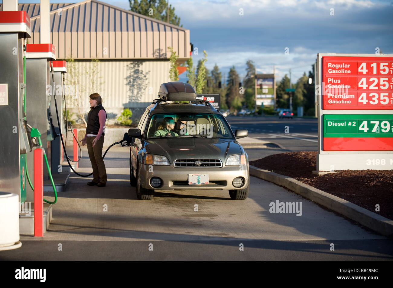 A young woman looking upset at the cost of gas while filling her car ...