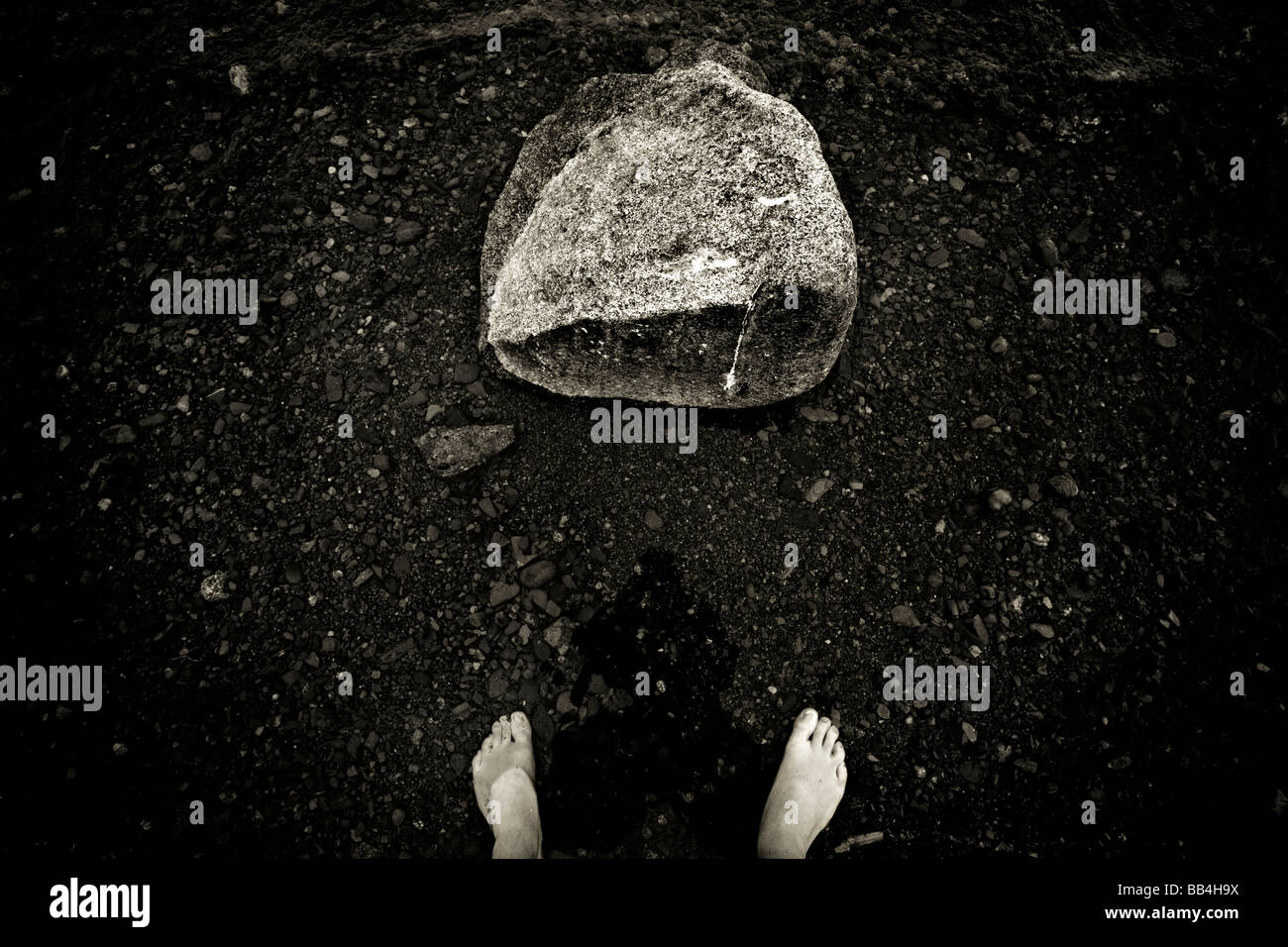 A man takes of photograph of his bare feet and a rock in the shallows ...