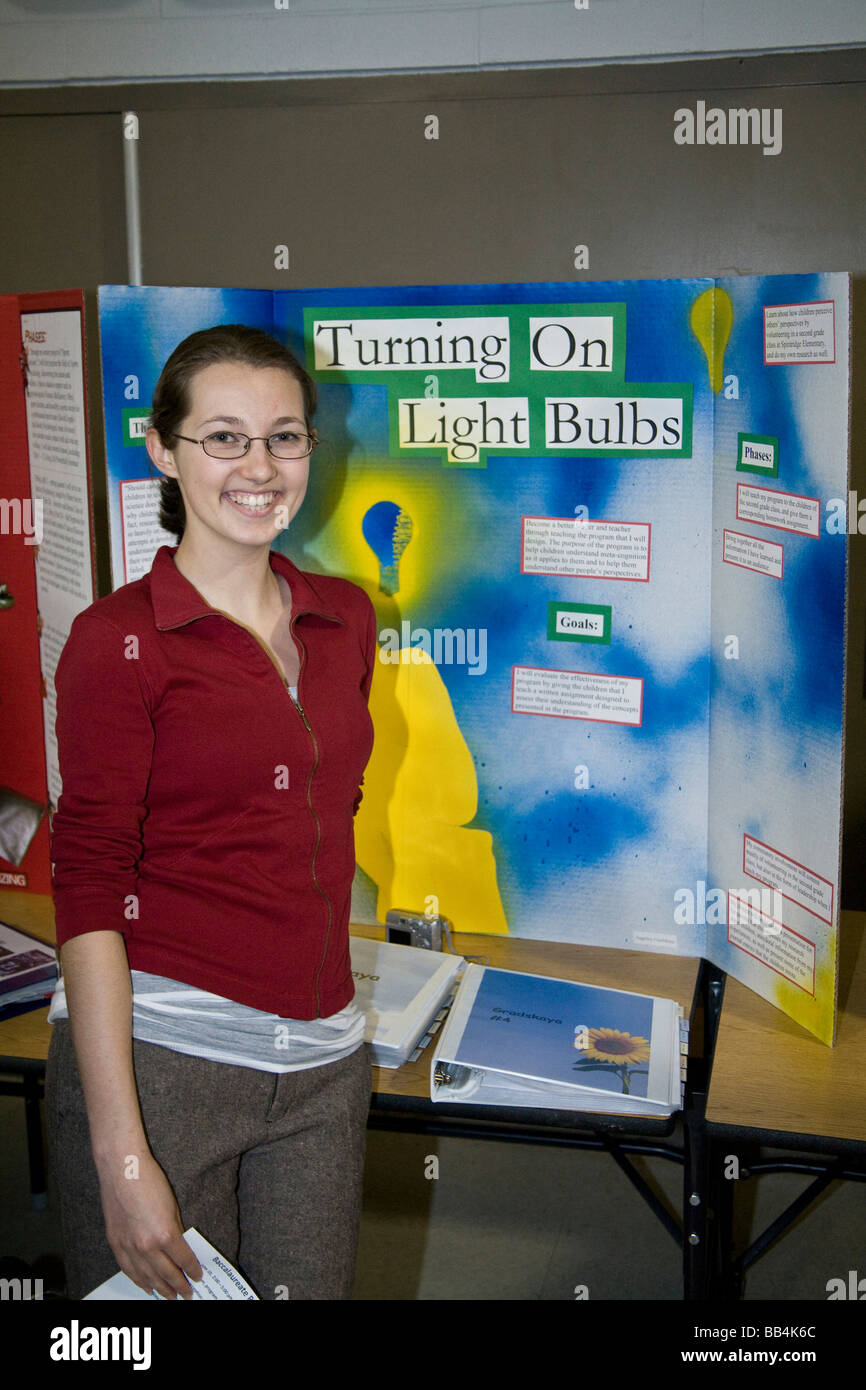 A teenage girl proudly displays her high school education fair project ...