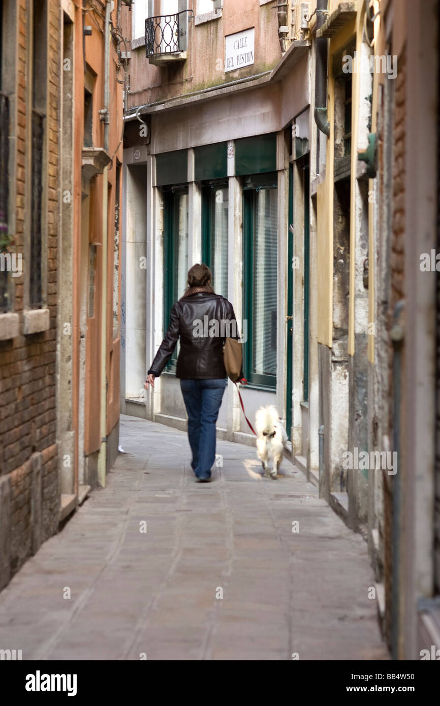 Europe, Italy, Venice. A woman walks her dog in the narrow city streets ...